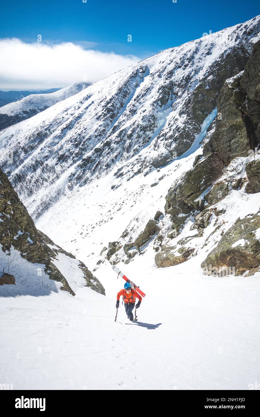 Man walking uphill with ice climbing tools and skis on his back Stock ...