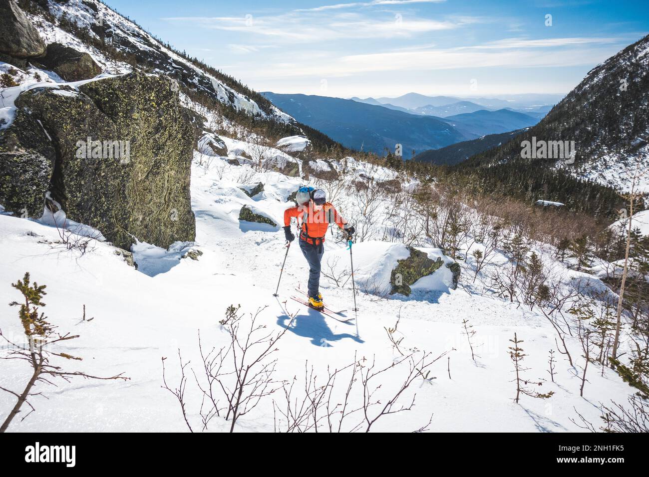 Man skiing uphill in snow surrounded by rocks and mountains Stock Photo ...
