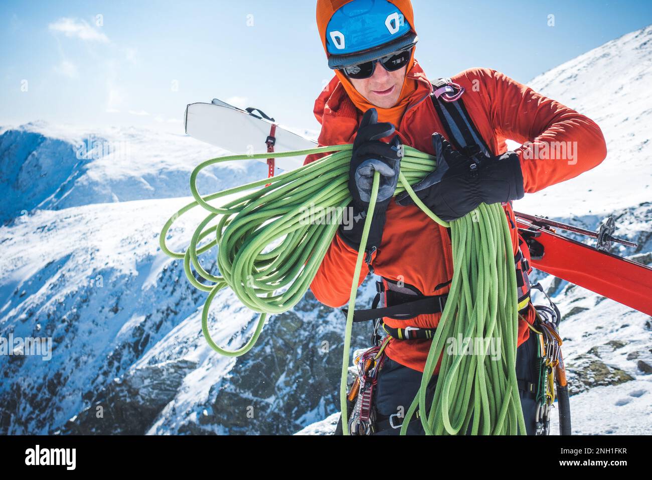 Ski mountaineer coiling rope with snowy mountains behind Stock Photo ...