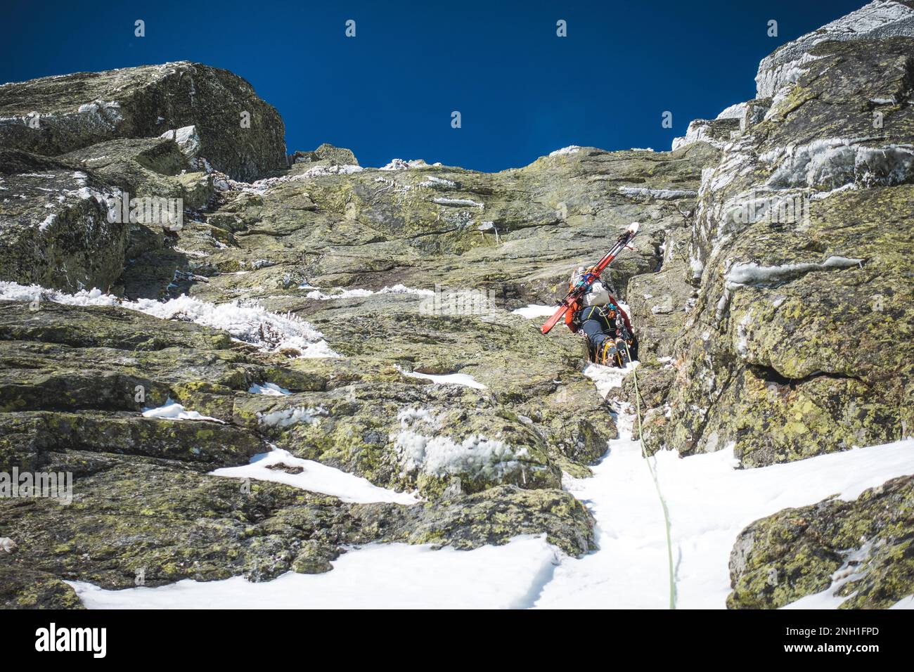 Ski mountaineer climbing thin ice patch on rock with skis Stock Photo ...