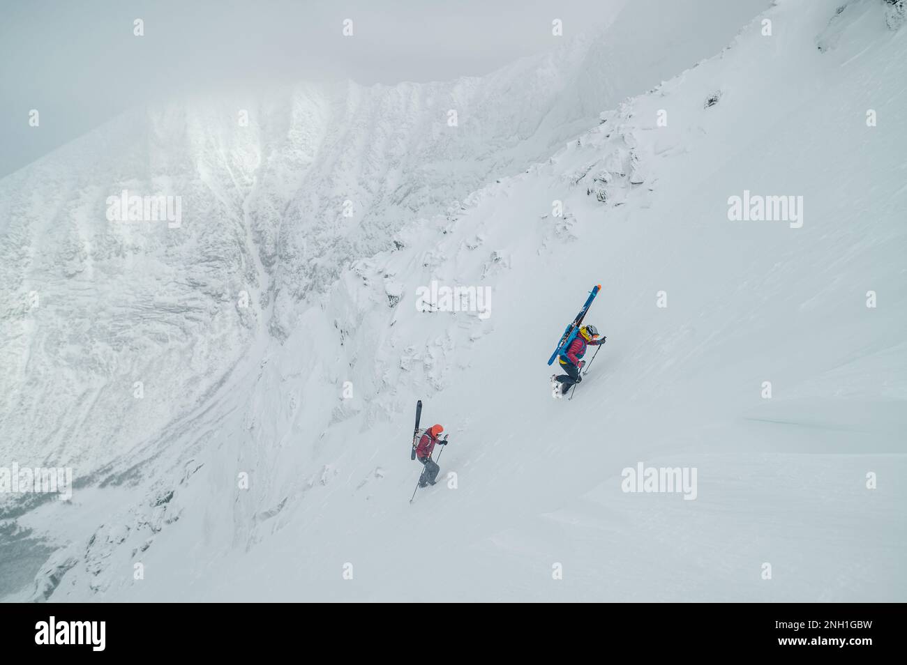 Backcountry skiers climbing steep gully with large mountains behind ...