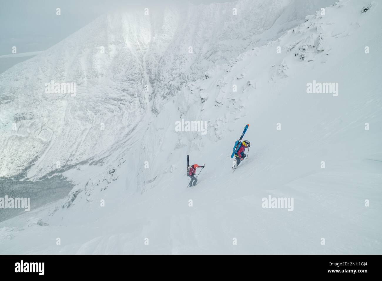 Backcountry skiers climbing steep gully with large mountains behind ...