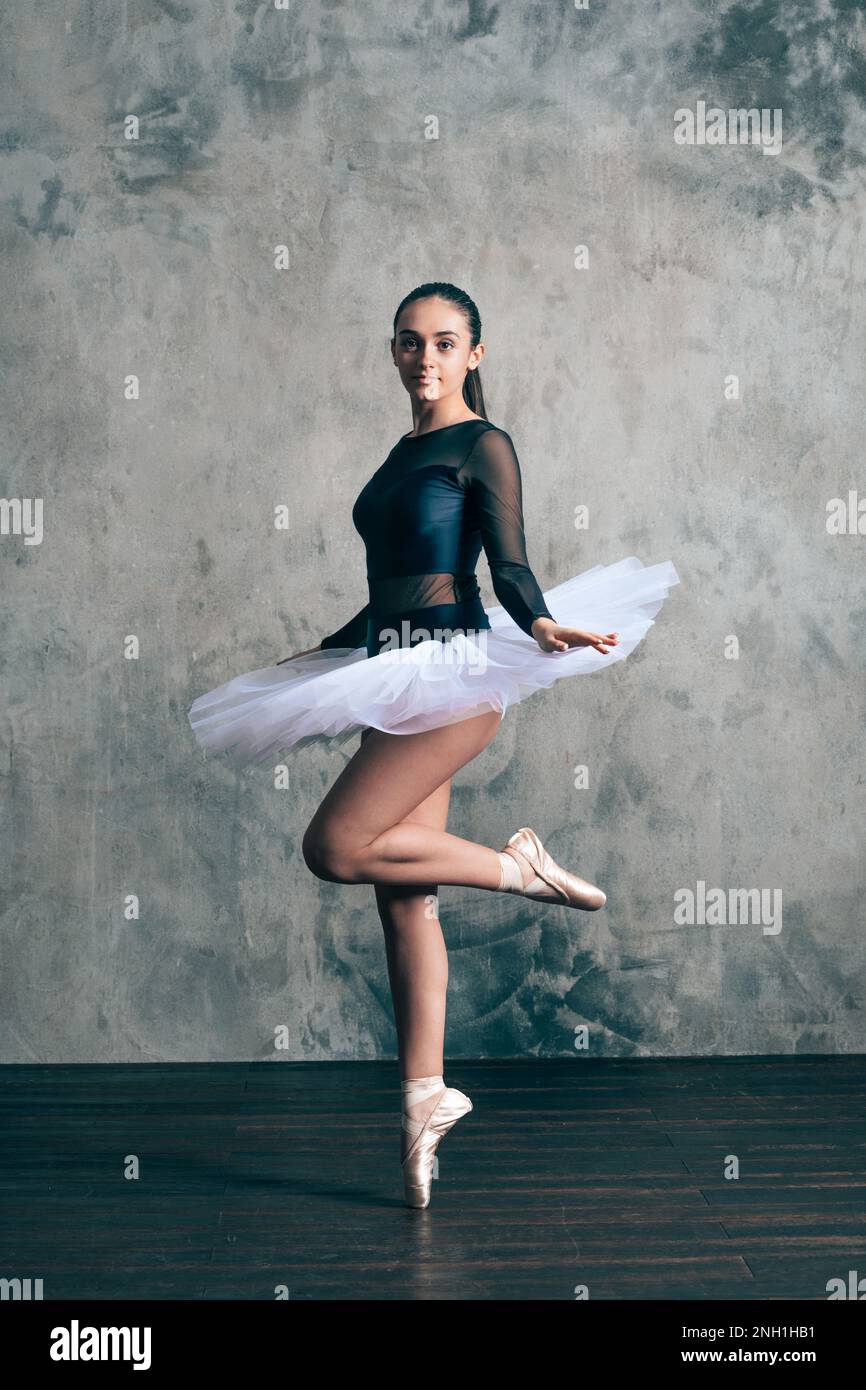 Full body of young slim ballerina in white tutu and pointe standing on ...