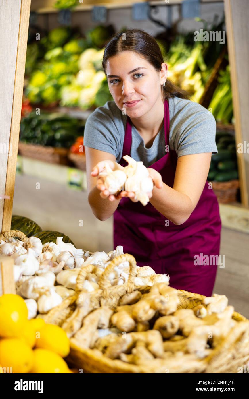 Woman seller wearing apron arranges garlic and other vegetables on ...