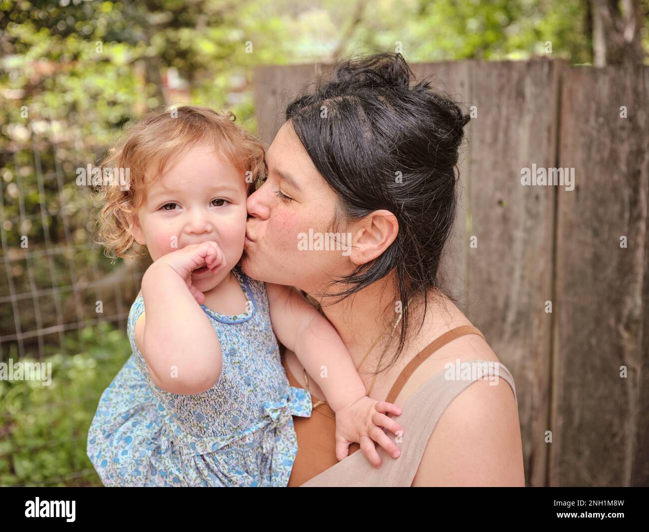 Mother kisses daughter on cheek, daughter looks at camera Stock Photo ...
