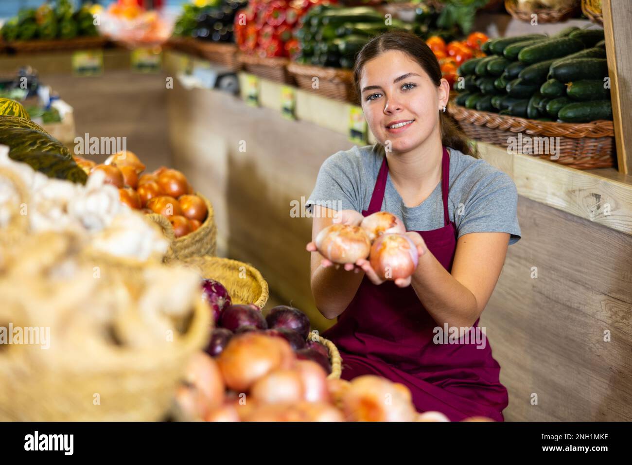 Female grocery store worker arranges red onion and other vegetables on ...