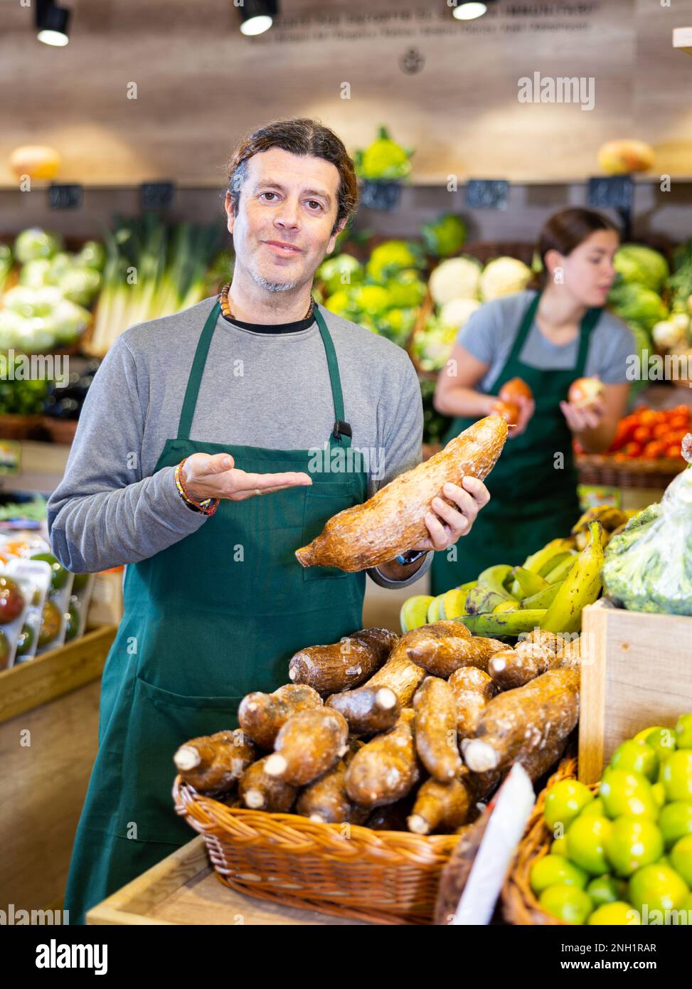 Male vegetable salesman in apron showing fresh yuca in market Stock ...