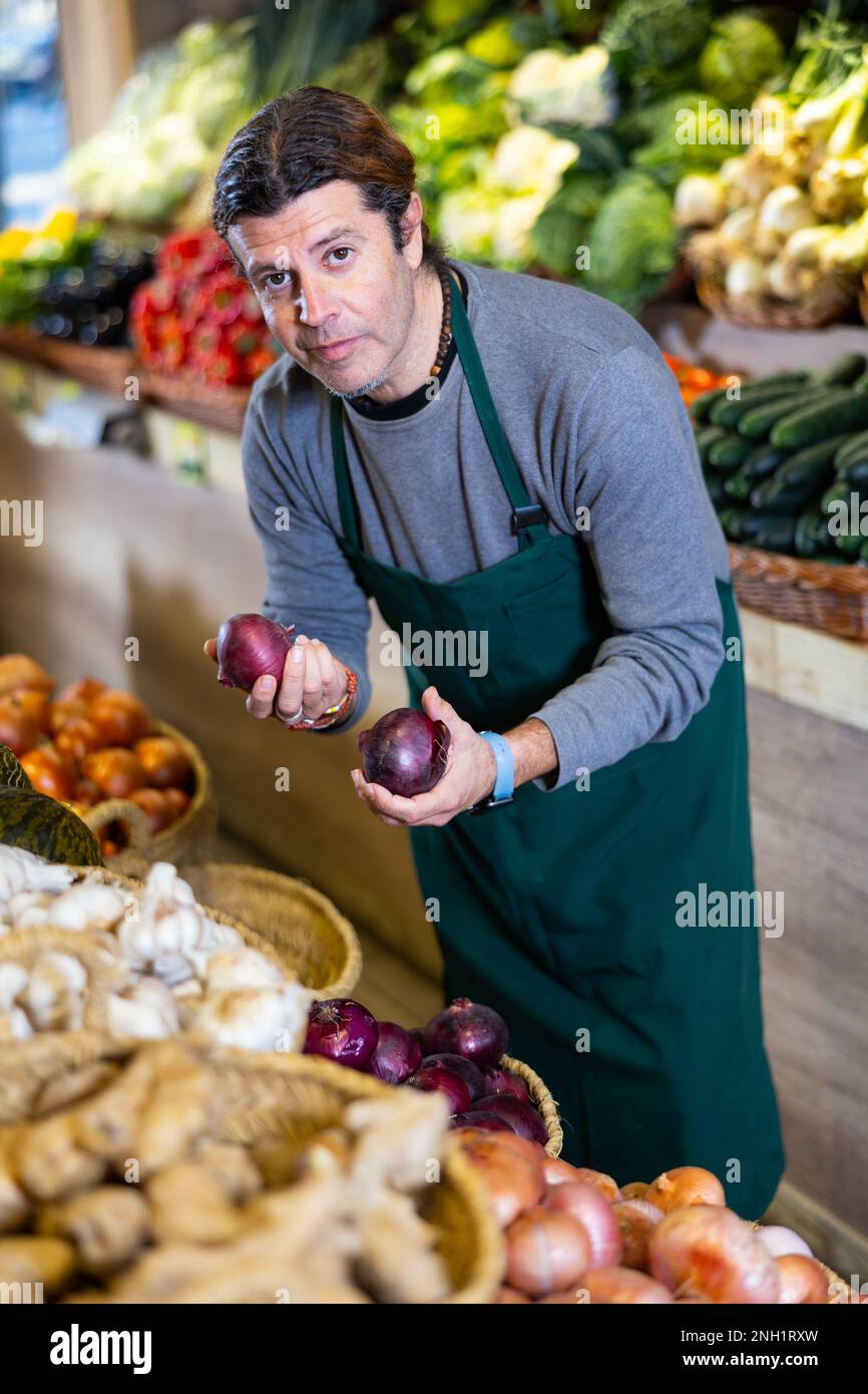 Male grocery store worker arranges red onion and other vegetables on ...