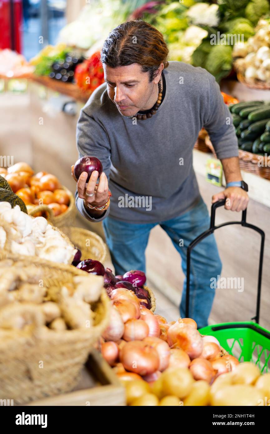 Man diligently picking out red onion to buy in vegetable aisle of ...