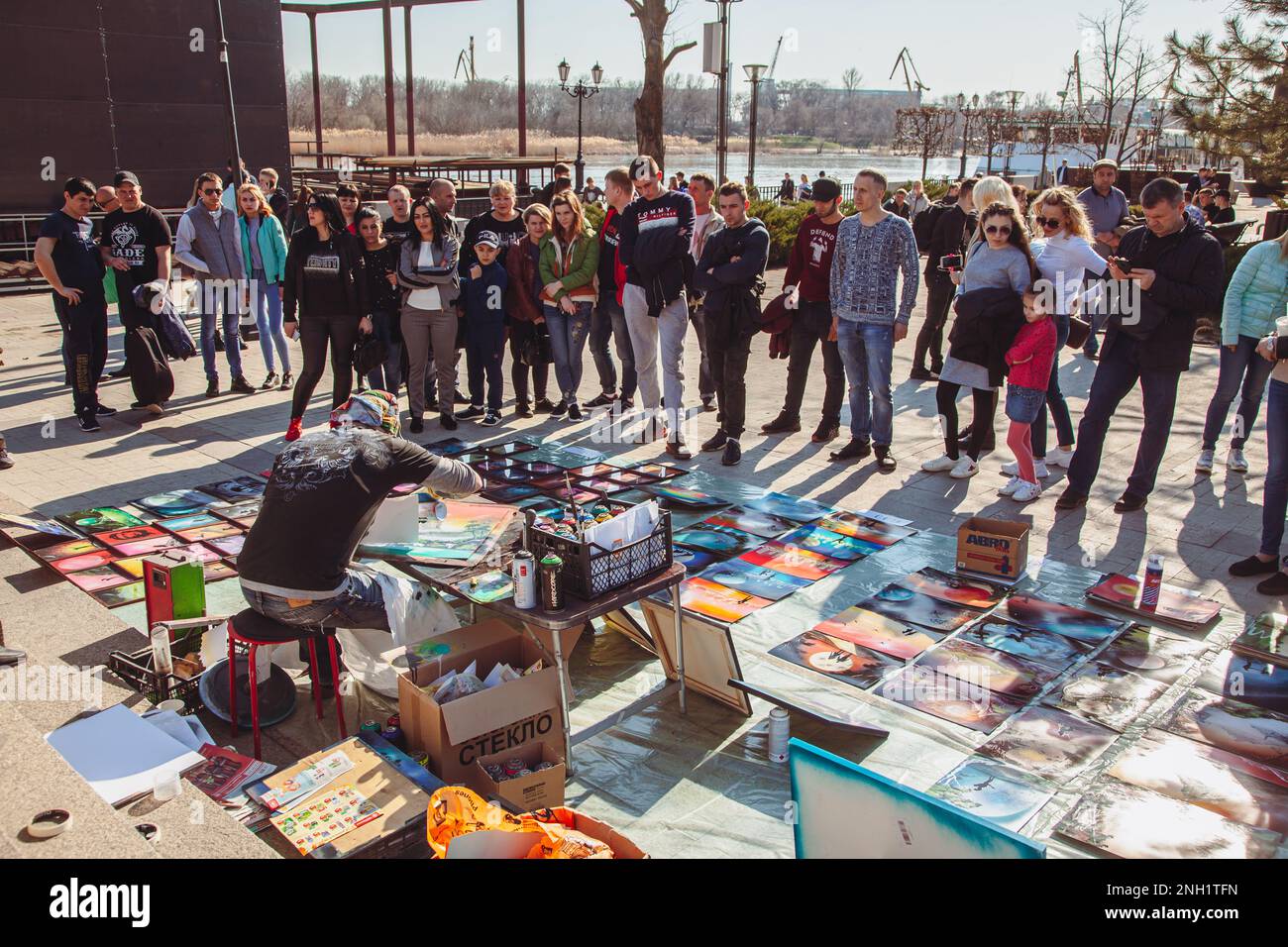 Artist on embankment, surrounded by crowd of people, draws in technique ...