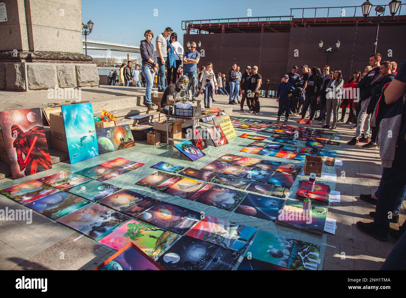 Artist on embankment, surrounded by crowd of people, draws in technique ...