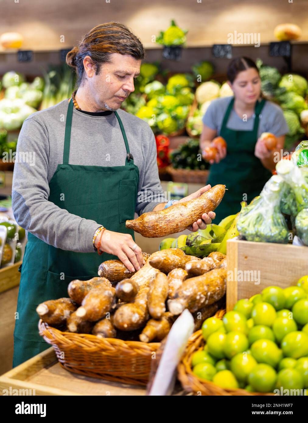 Male vegetable salesman in apron showing fresh yuca in market Stock ...