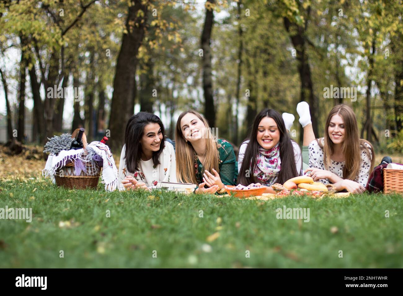 Group of four women having a fun picnic in the park, laying on a ...