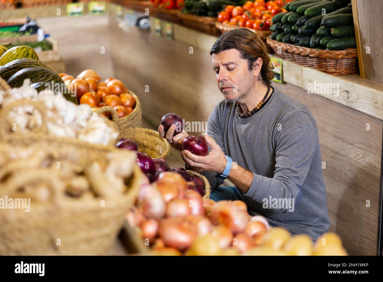 Man diligently picking out red onion to buy in vegetable aisle of ...