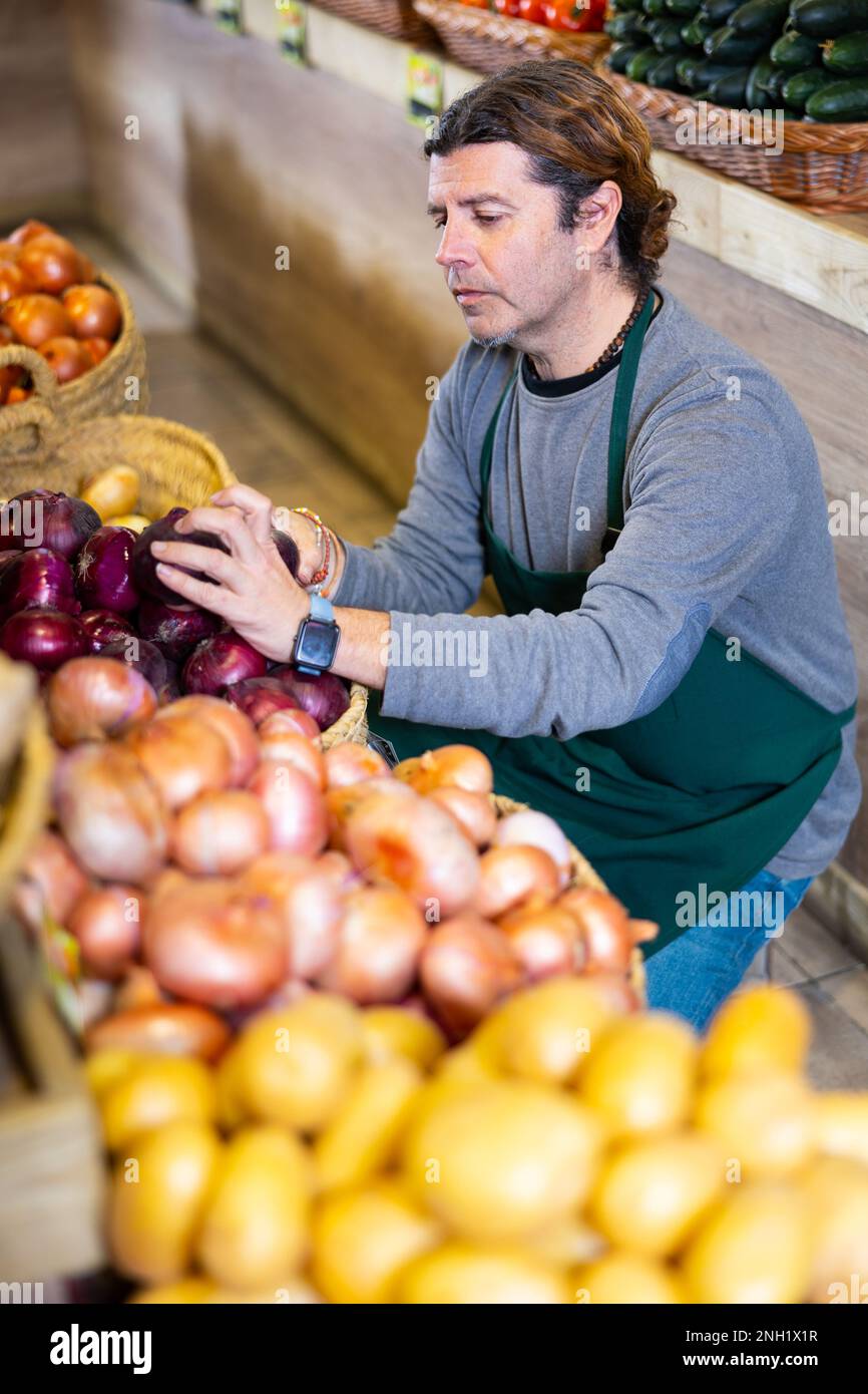 Male grocery store worker arranges red onion and other vegetables on ...
