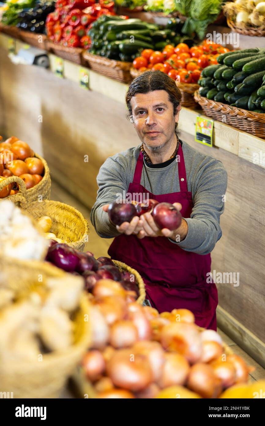 Male grocery store worker arranges red onion and other vegetables on ...