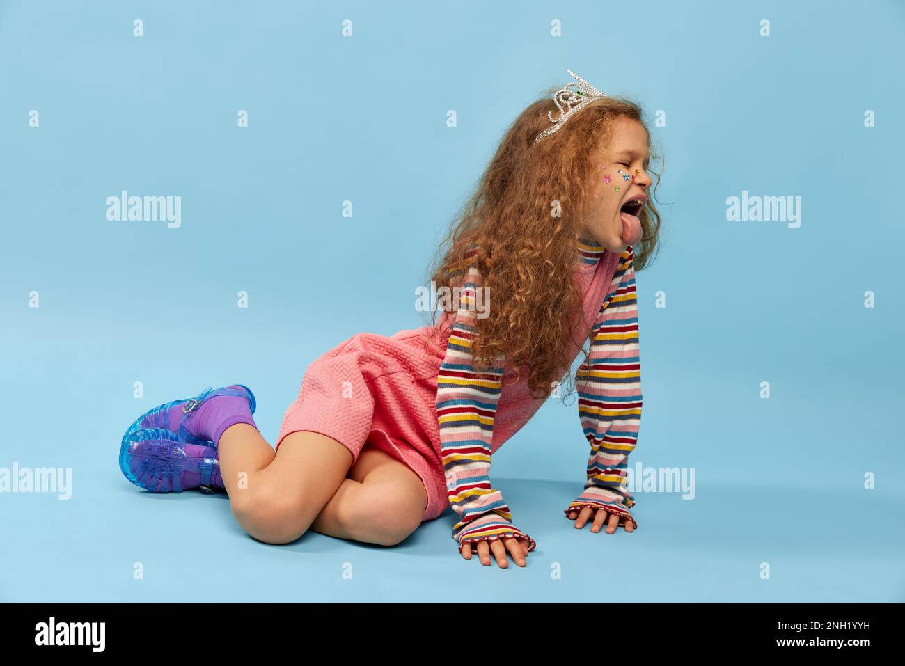 Grimacing, tongue sticking out. Little cute girl, child with curly hair posing in pink dress ...