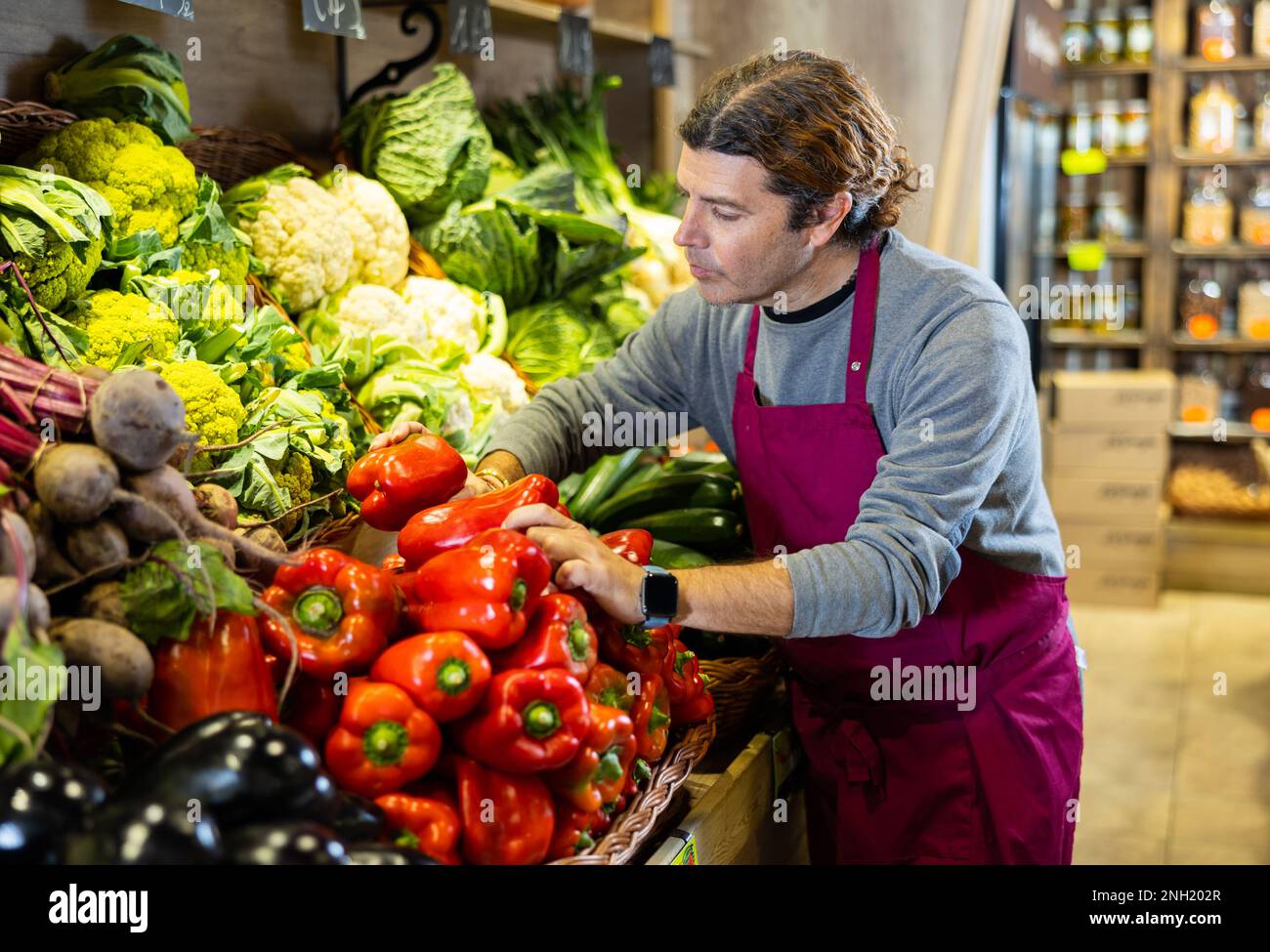 Male grocery store worker arranges bell peppers and other vegetables on ...