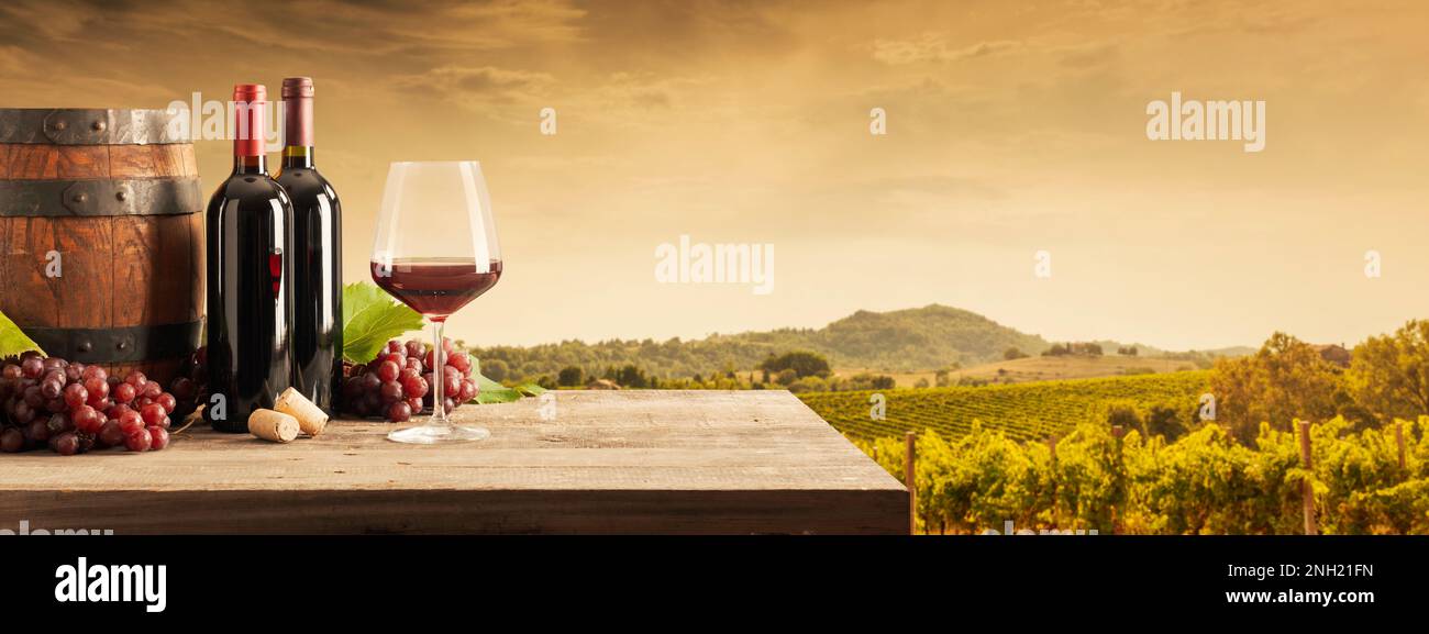 Red wine bottles, wine glass, barrel, grapes and vineyard in the ...