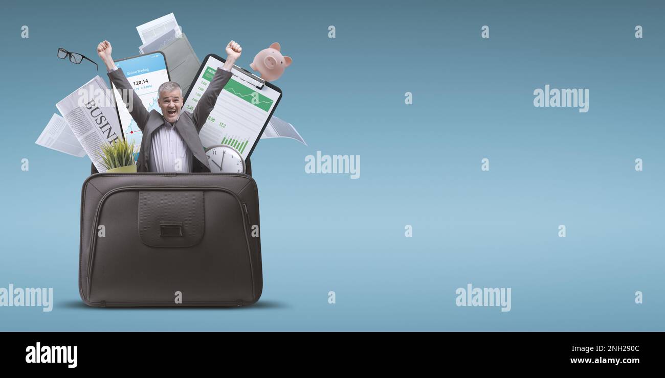 Cheerful businessman celebrating with arms raised and office items in a ...