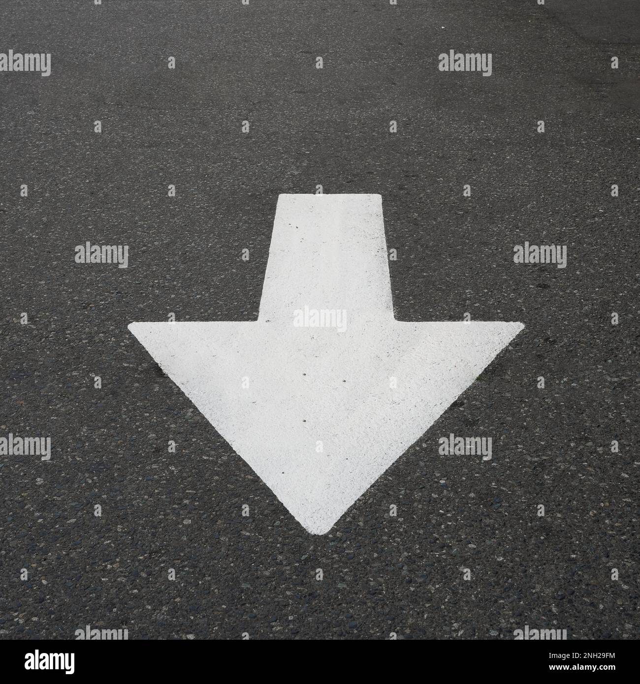 White traffic arrow on the grey asphalt directs vehicles to drive in a ...