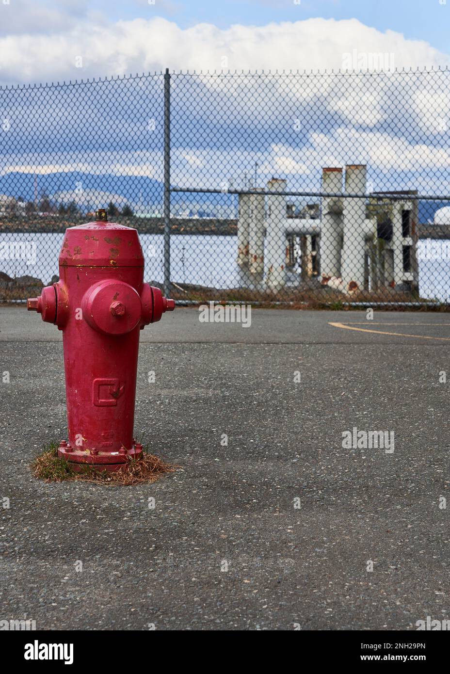 A close up of a red fire hydrant in a parking lot beside the ocean and ...