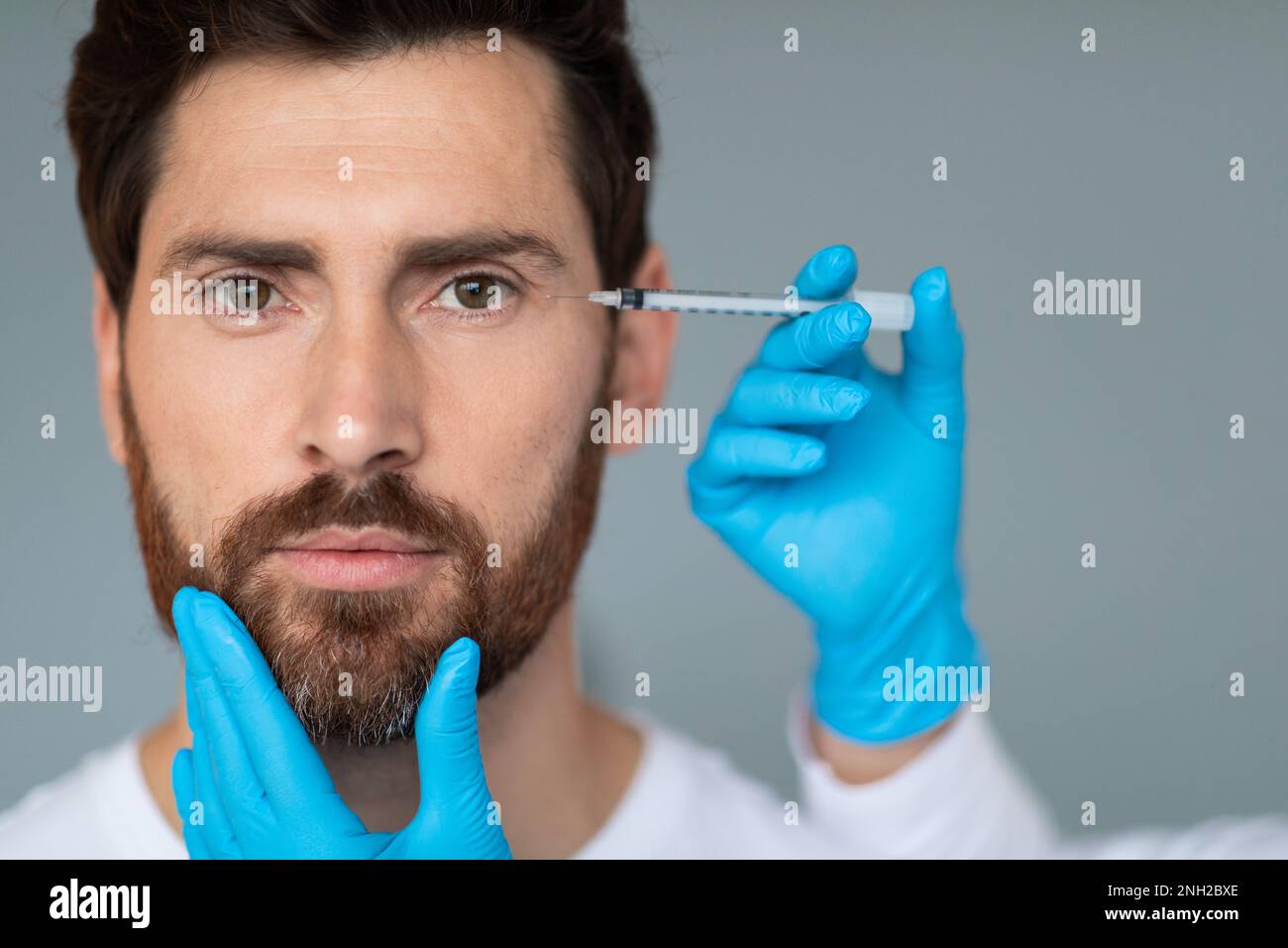 Middle aged man receiving beauty shot from cosmetologist on grey studio ...