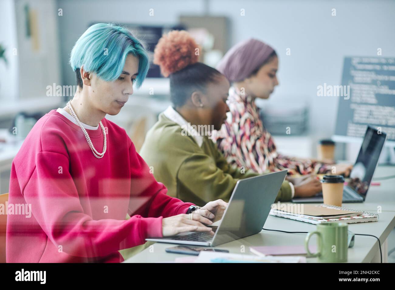 Diverse team of gen Z software developers using computers behind glass ...