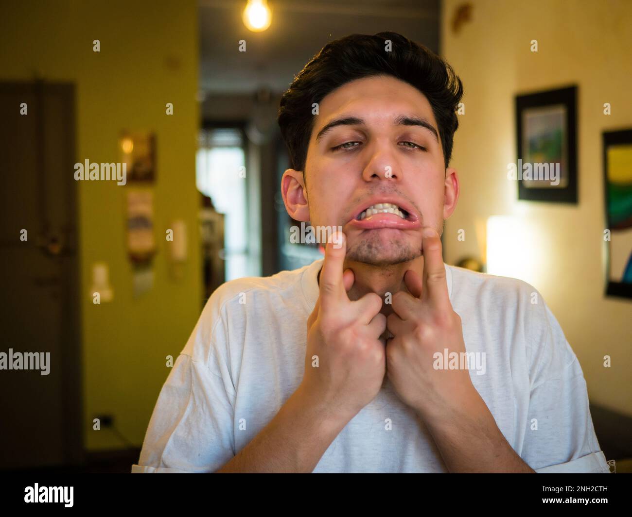 Young man pulling corners of lips down making unhappy facial expression ...