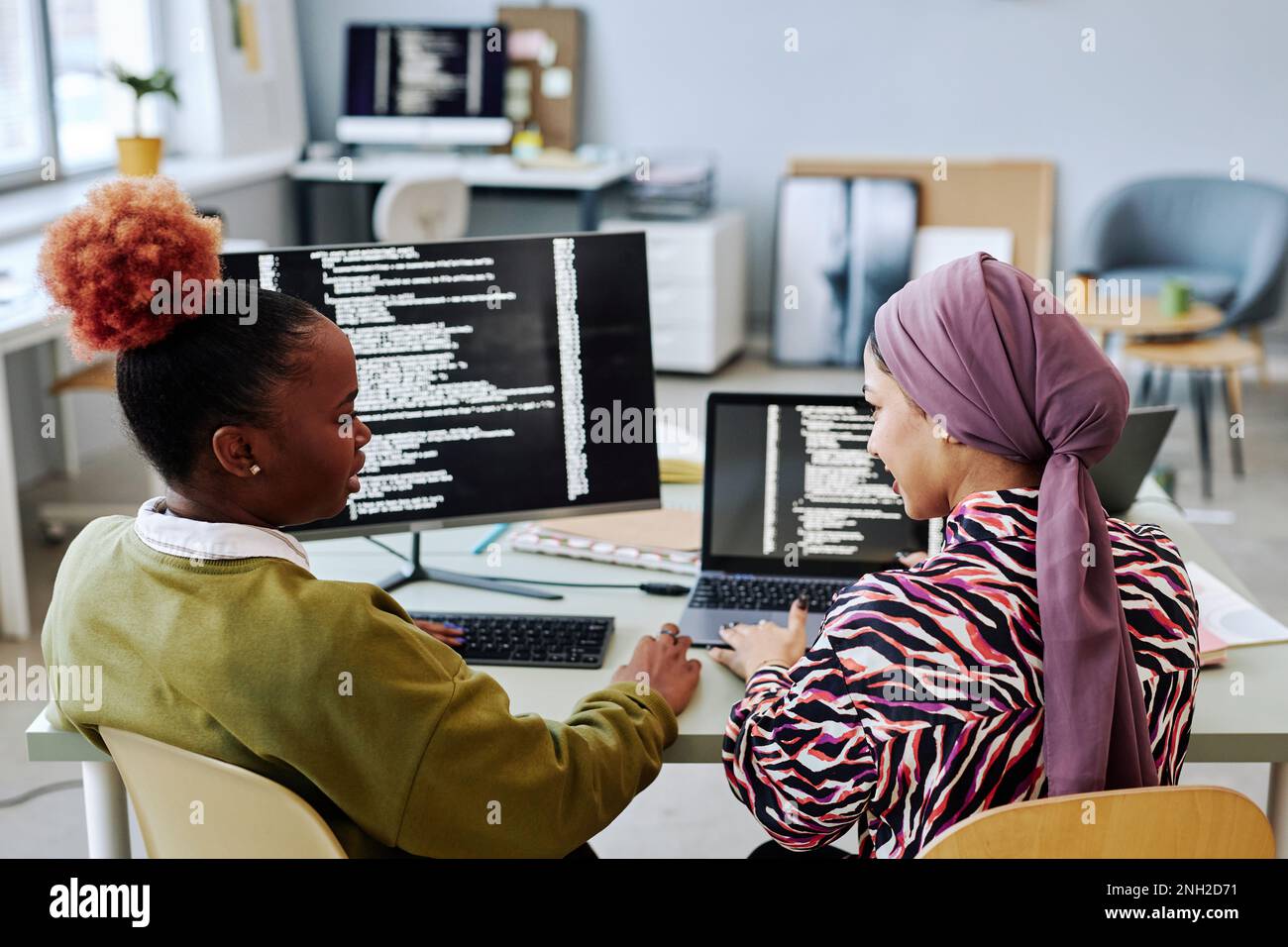Back view at two female programmers writing code and discussing project ...