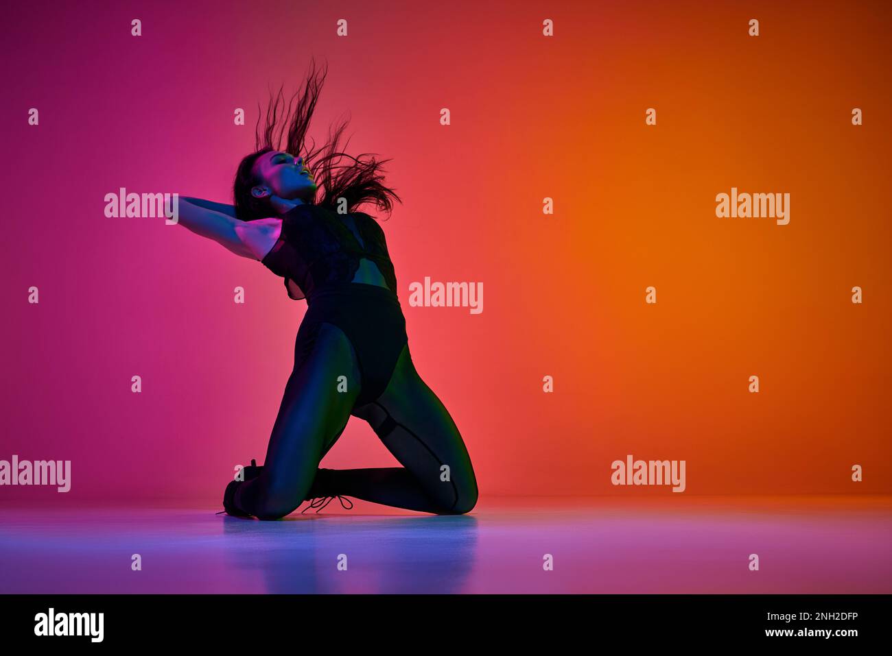 Self-expression through movements. Young woman dancing high heel dance style over gradient pink ...