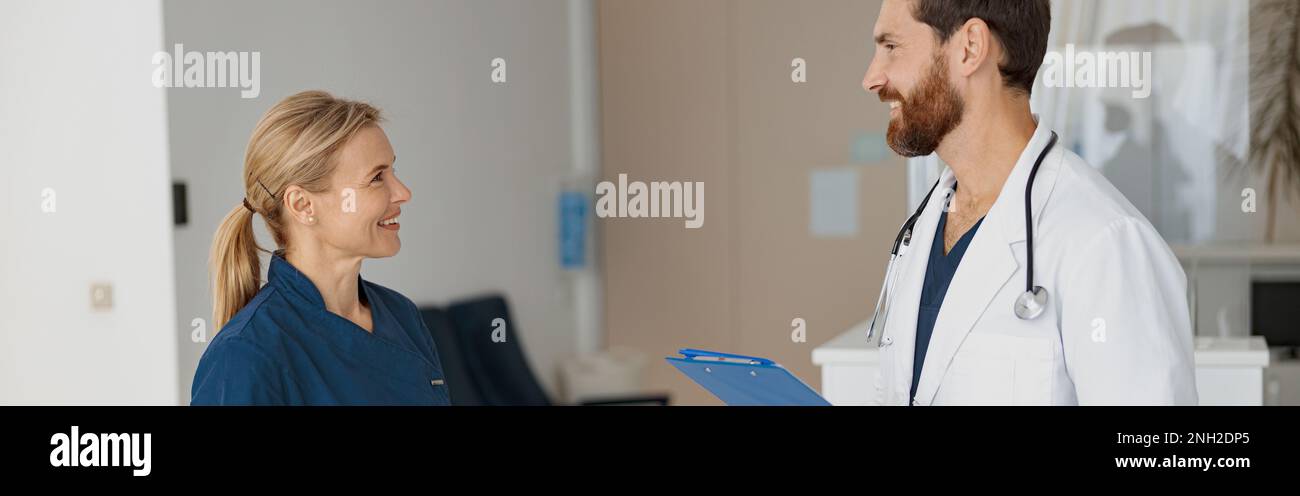 Two doctor colleagues talking during break standing in clinic hall ...