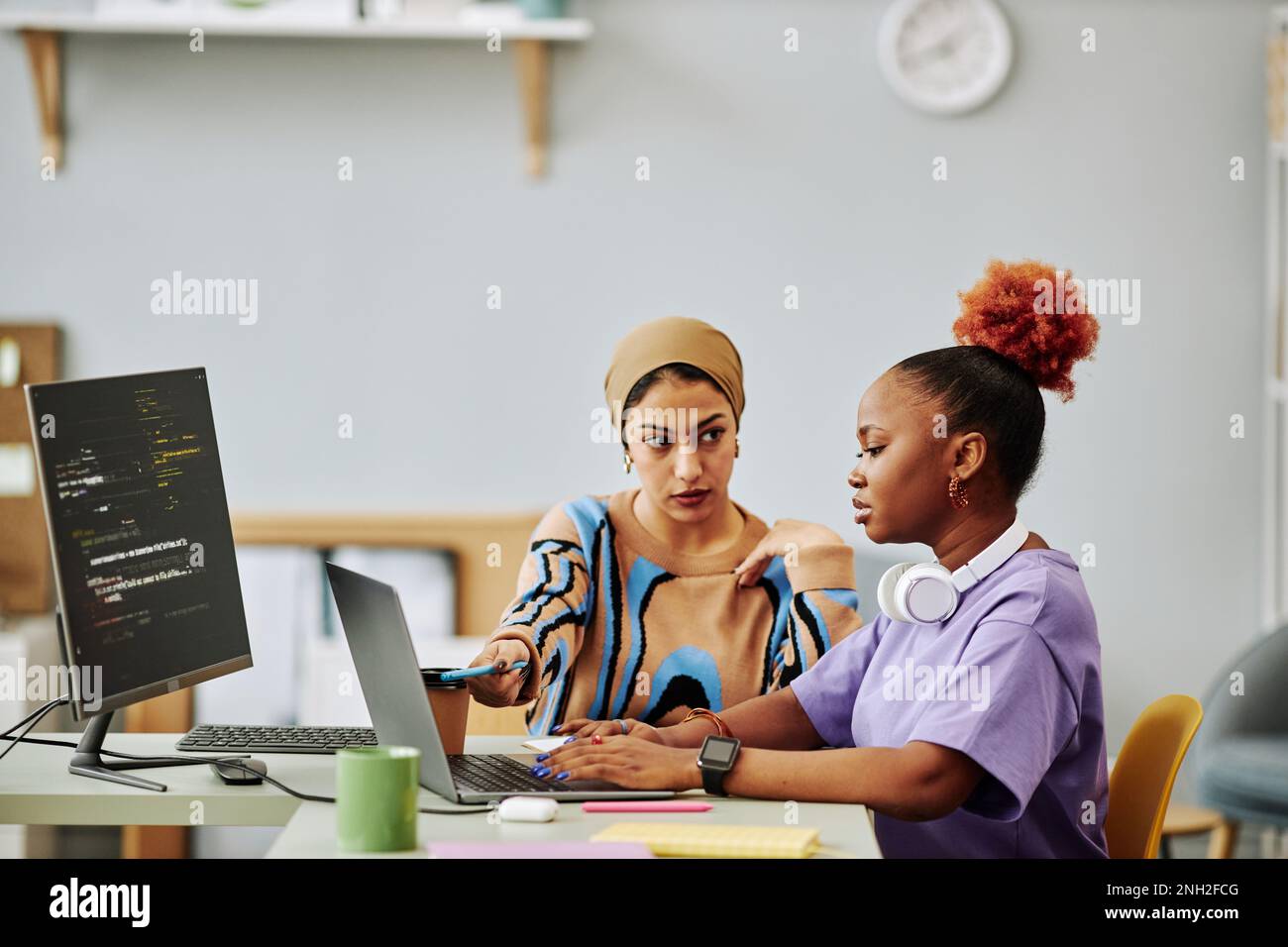 Portrait of two ethnic young women using computer while working on ...