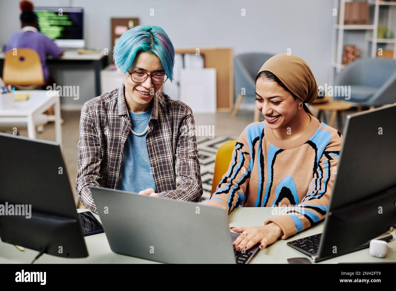 Portrait of two young software developers using computers in office and ...