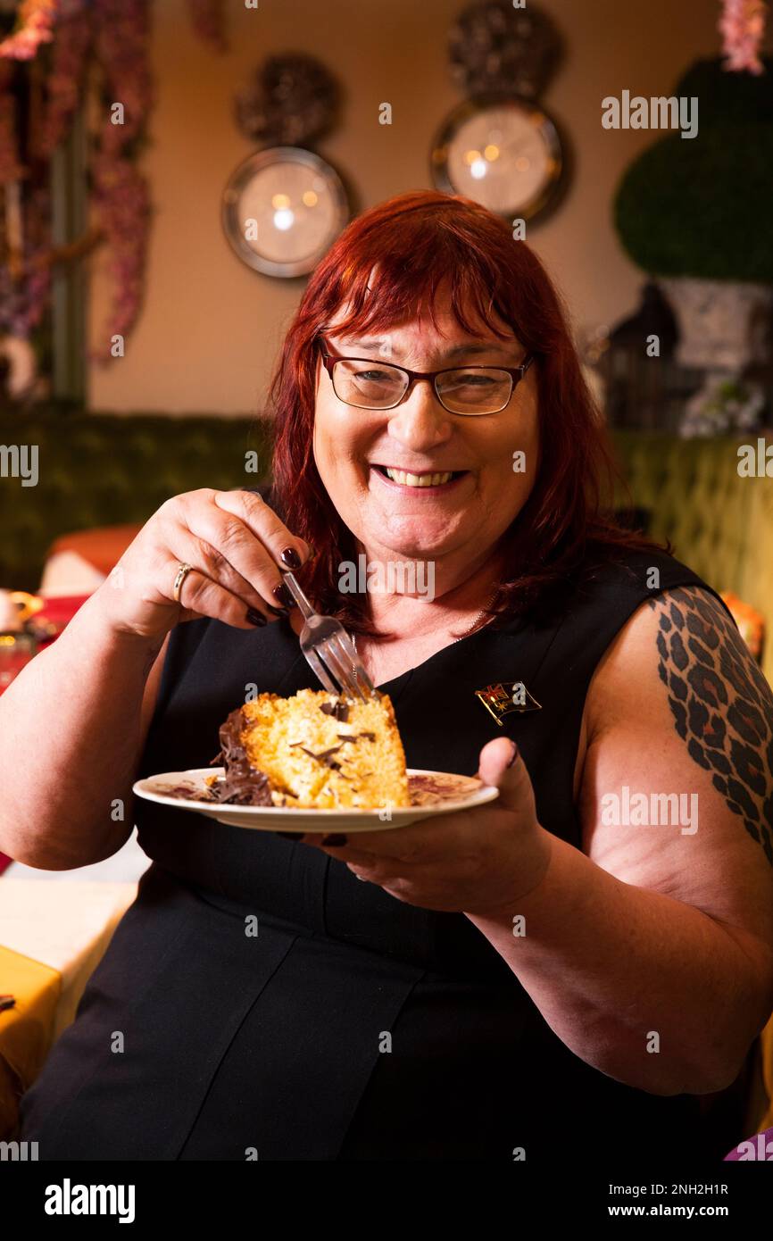Woman relaxing in a colourful, cosy cafe eating a large piece of cake ...