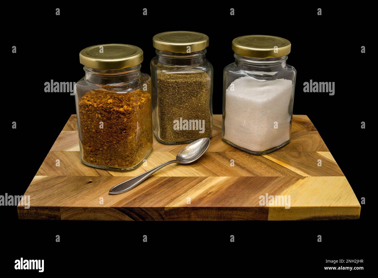 Three glass jars with different spices on a wooden board with spoon ...