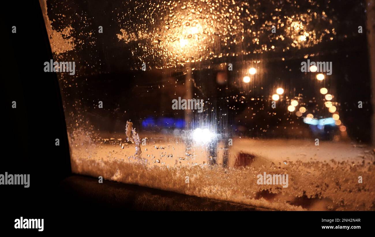 Misted car window. Melting snow on a car window. Car headlights, bokeh ...