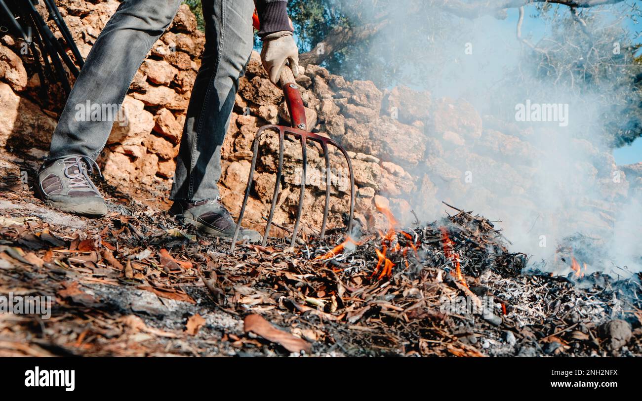 closeup of a man burning branches and other plant remains after the ...