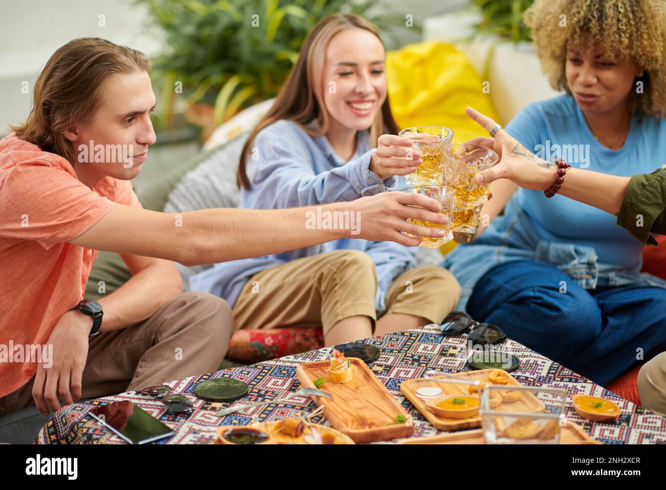 Group of young people toasting with glasses of beer over table with ...