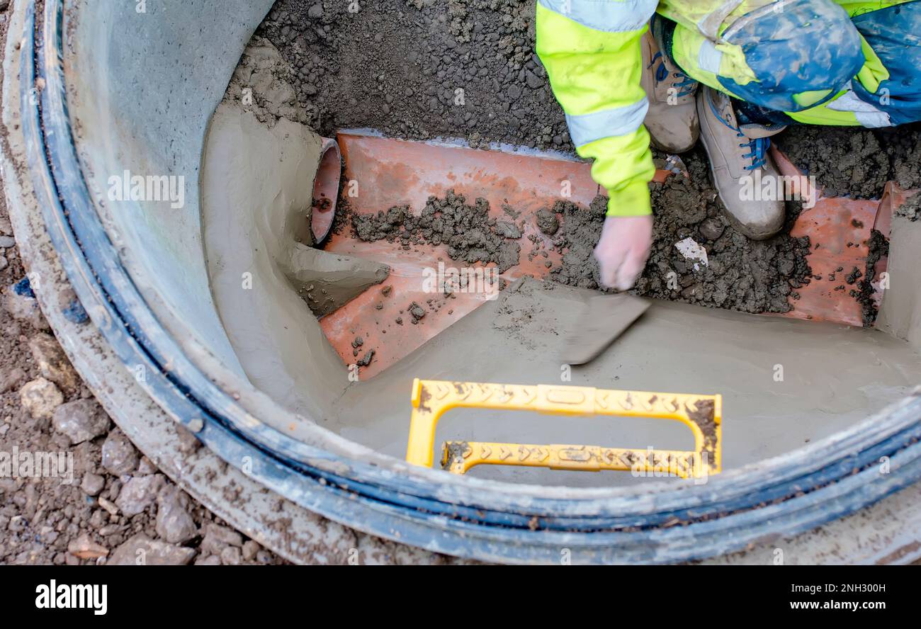 A builder in the new built manhole benching it with sand and cement mix ...