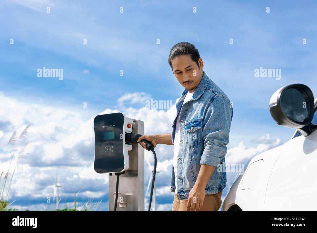 Progressive man with electric vehicle and cloudscape background. EV car ...