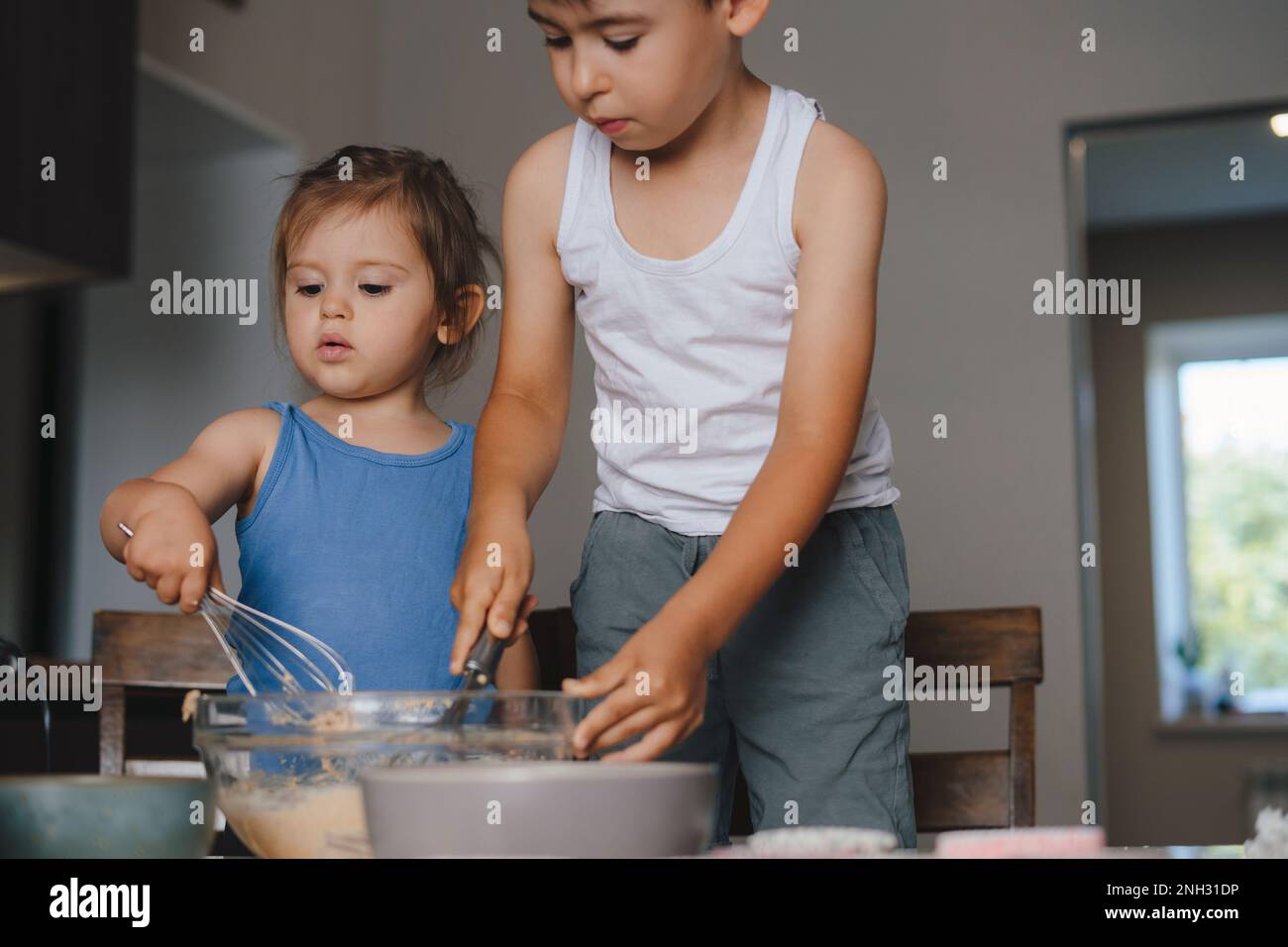Brother and sister standing at the kitchen table mixing ingredients for ...