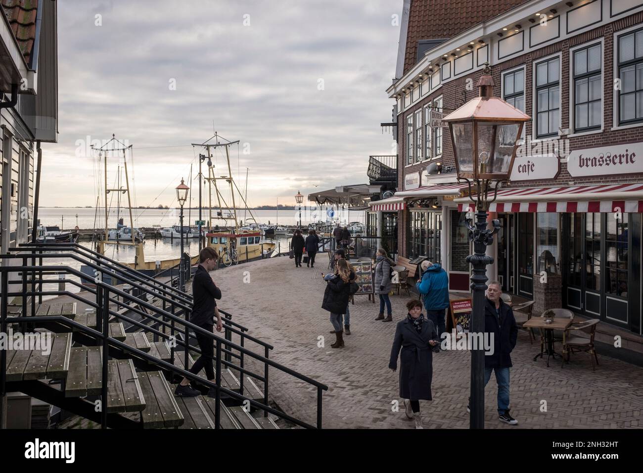 Tourists walk by cafes on the waterfront promenade in the winter, in ...