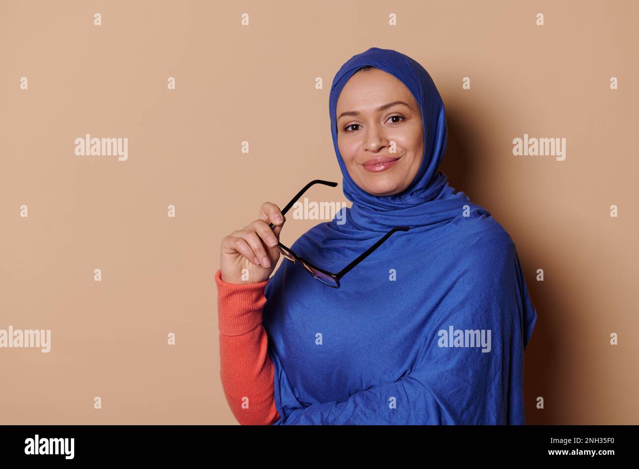 Beautiful Muslim woman in blue hijab, holding stylish eyeglasses in her ...