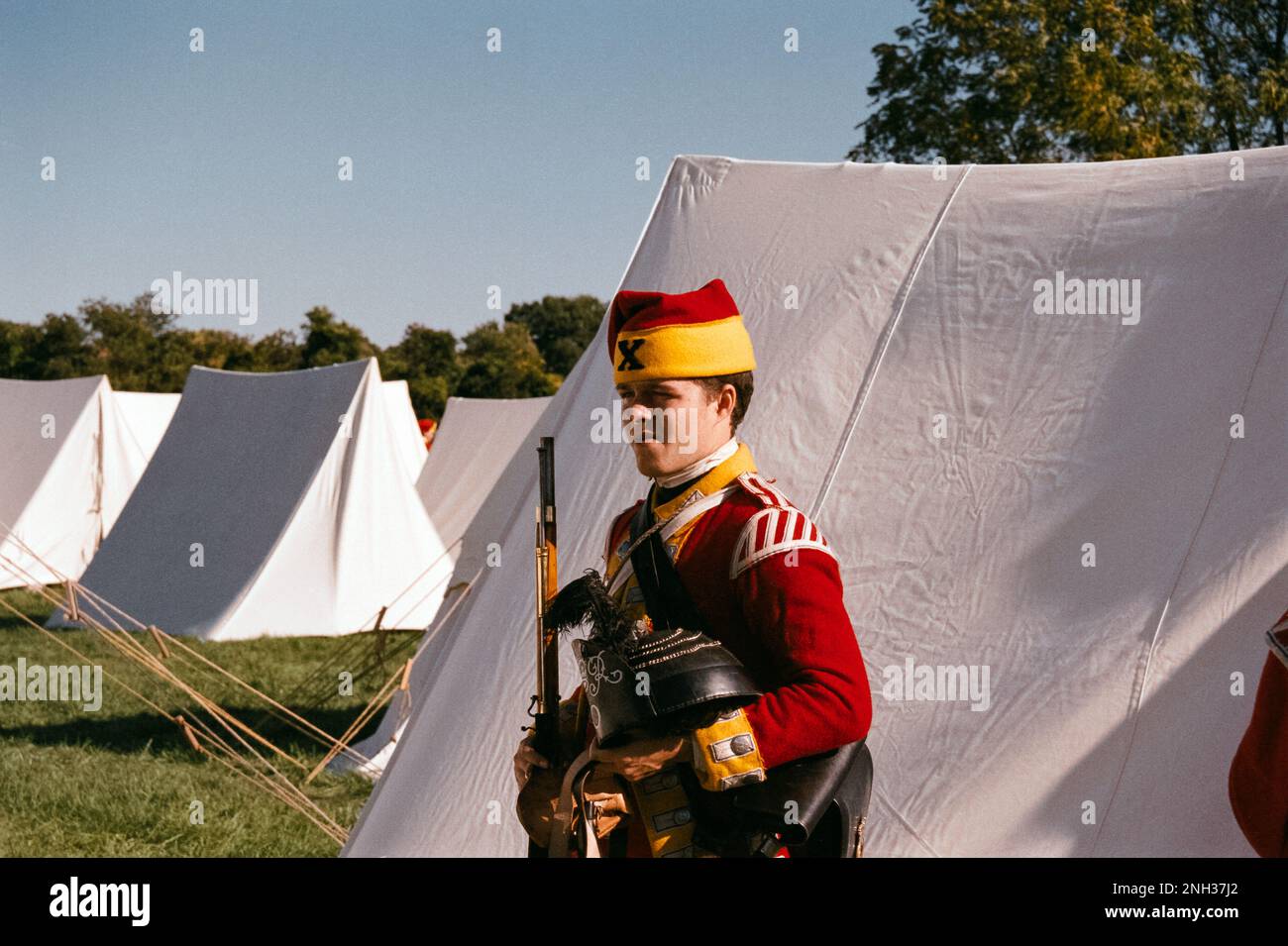 A Red Coat (British) soldier stands guard with musket in tent camp ...