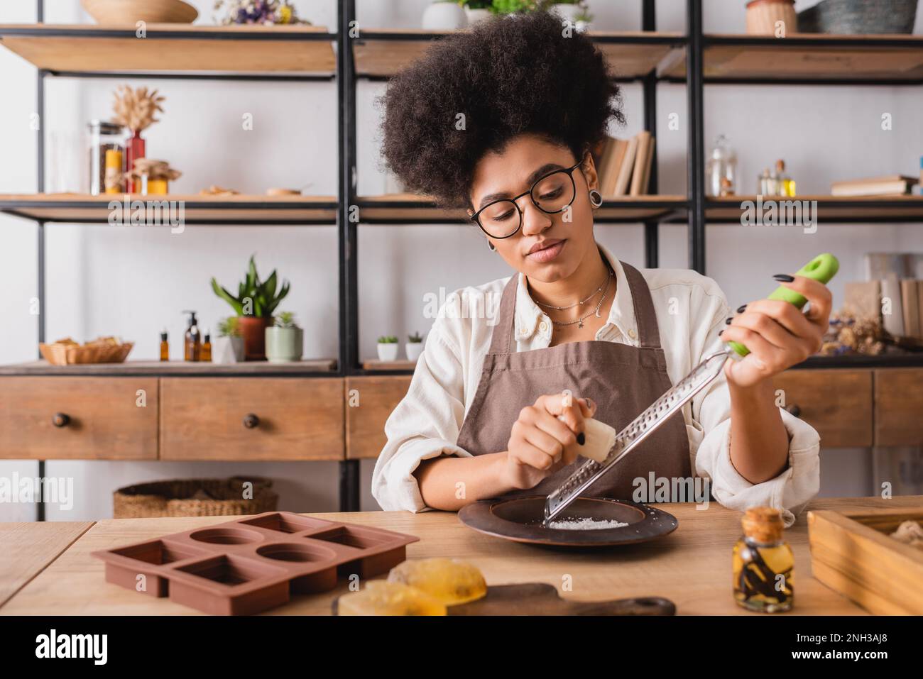african american craftswoman in eyeglasses grating soap bar near ...