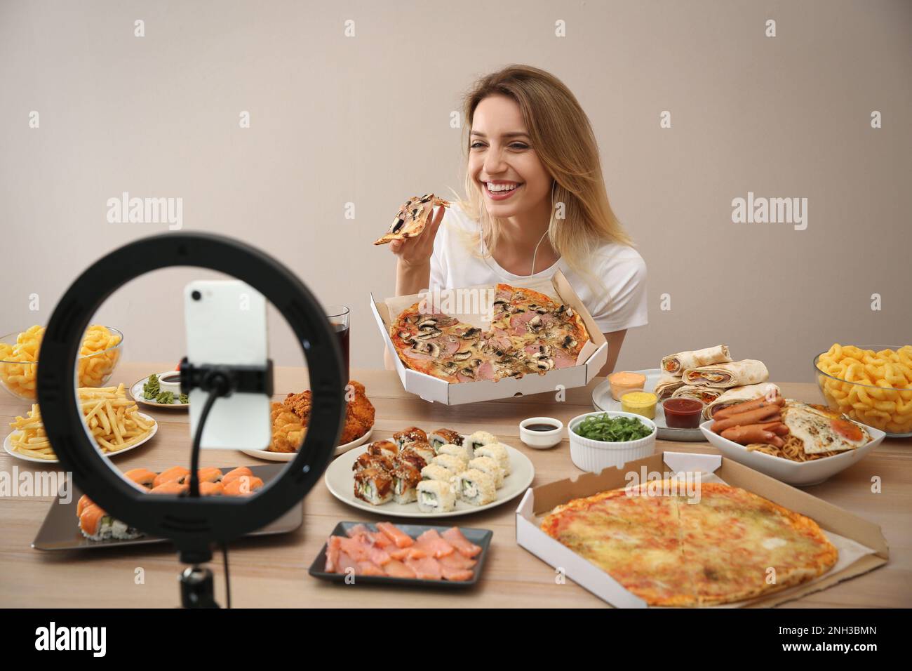 Food blogger recording eating show on smartphone camera against beige ...