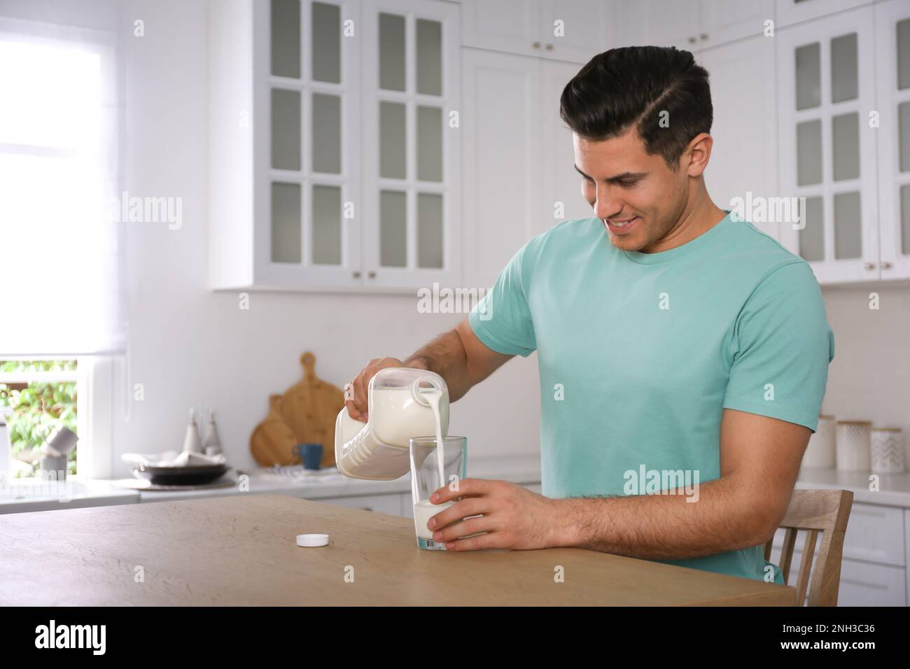 Man pouring milk from gallon bottle into glass at wooden table in ...