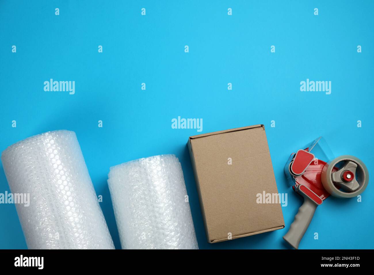 Bubble wrap rolls, cardboard box and tape dispenser on light blue ...