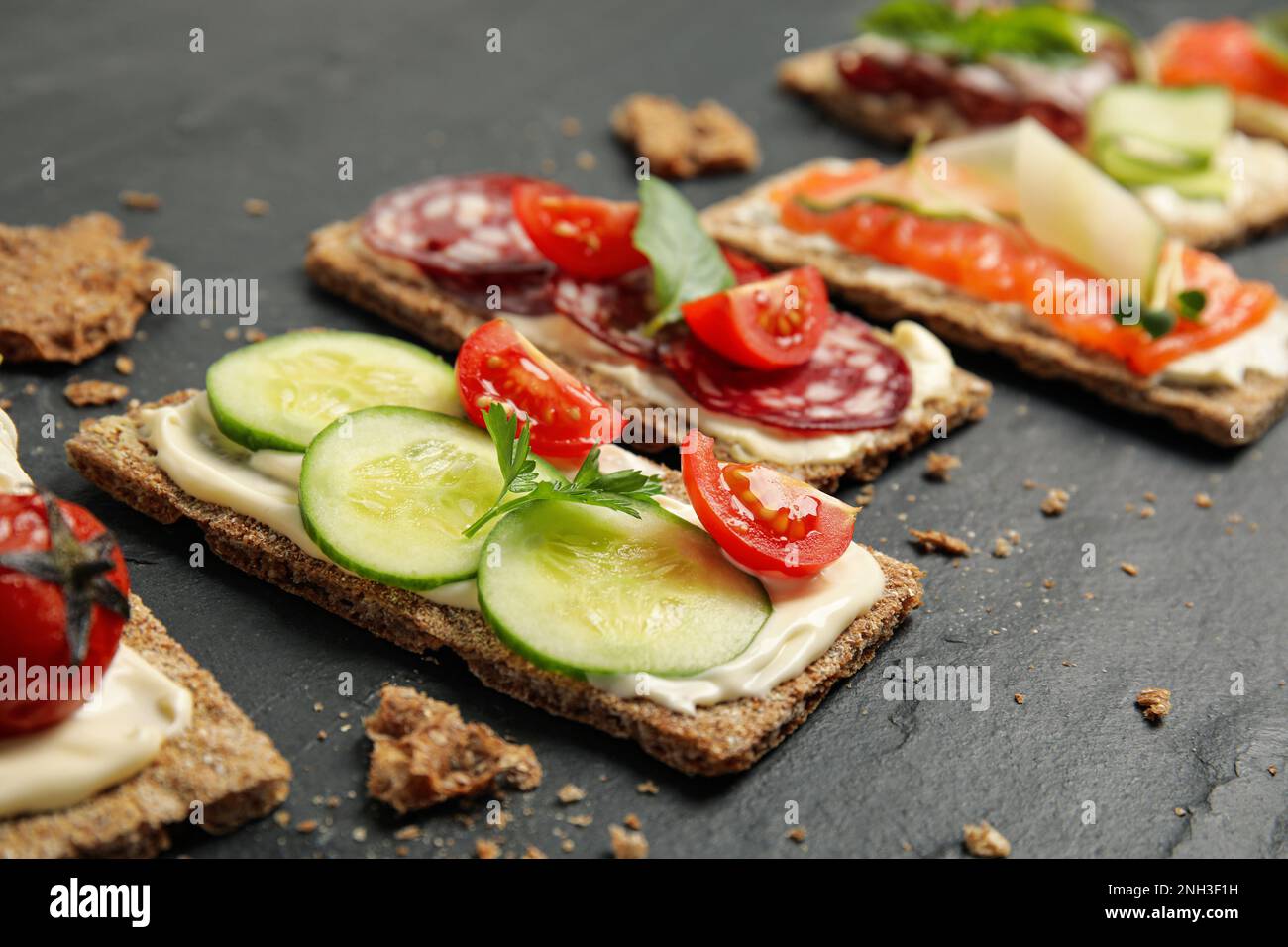 Fresh rye crispbreads with different toppings on black table, closeup ...